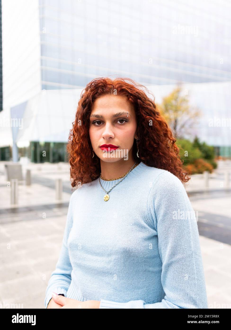 Self assured young woman with long curly red hair in casual clothes ...