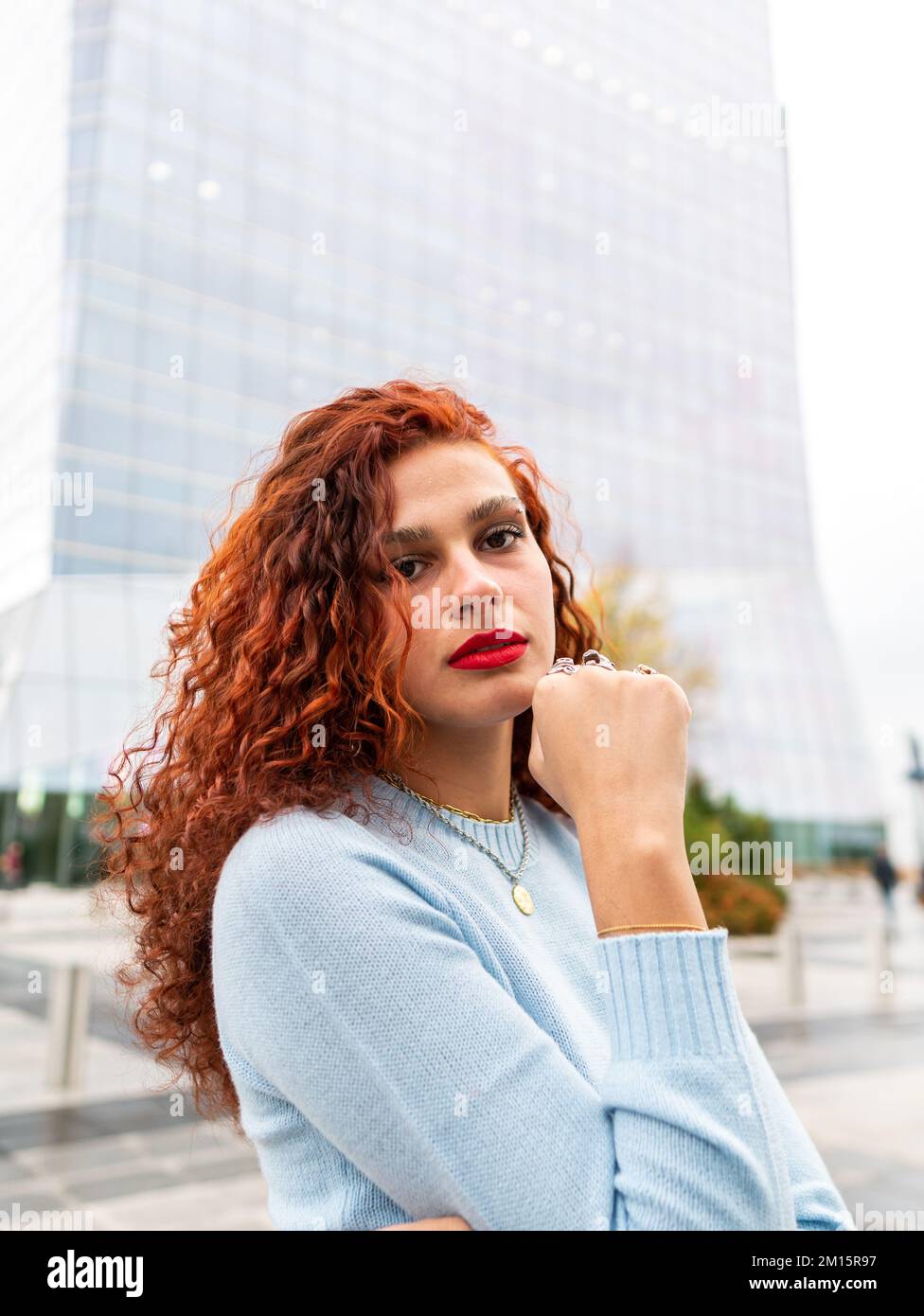 Self assured young woman with long curly red hair in casual clothes ...