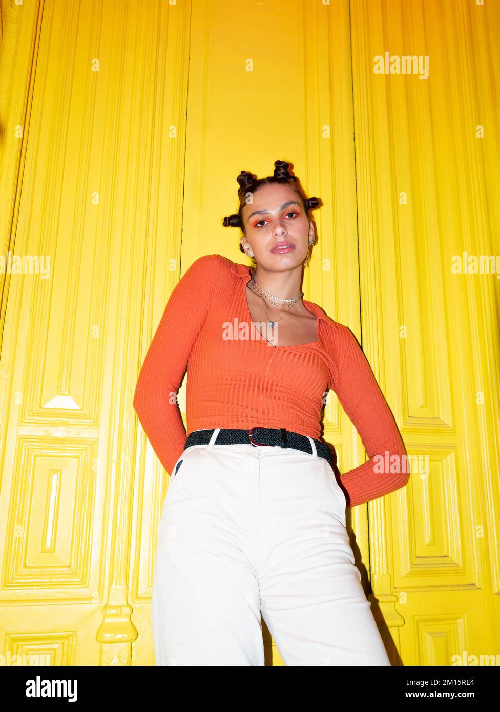 From below portrait of serious young woman with bantu knots and orange ...