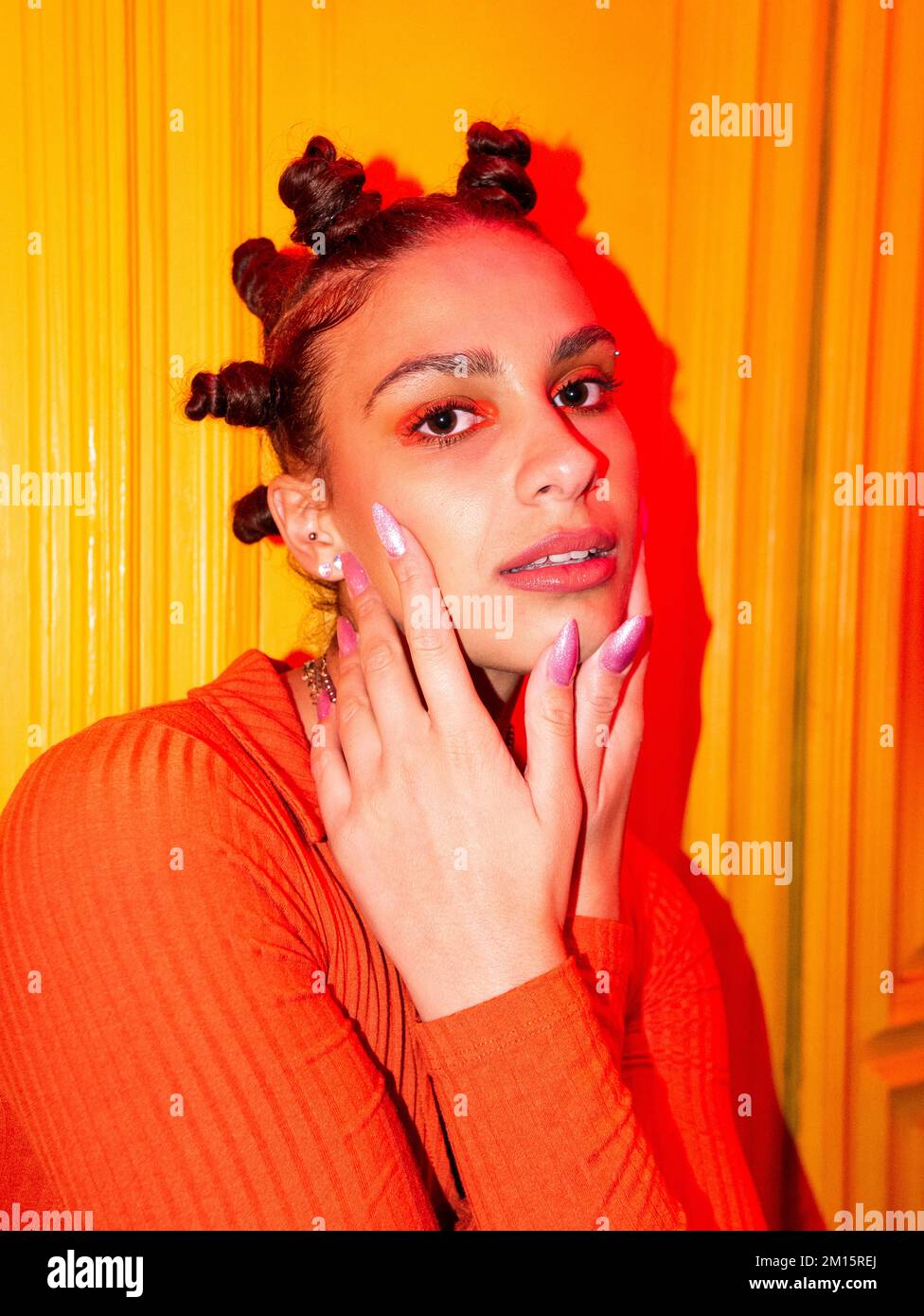 Charming young female with long nails and bantu knots in orange sweater ...