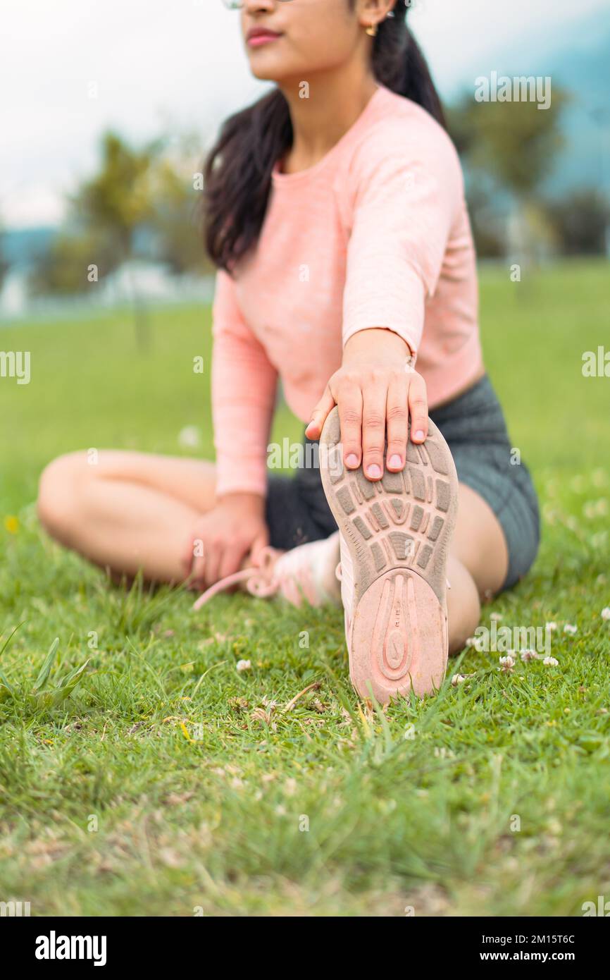 Crop young female in sportswear and sneakers sitting on grass while ...