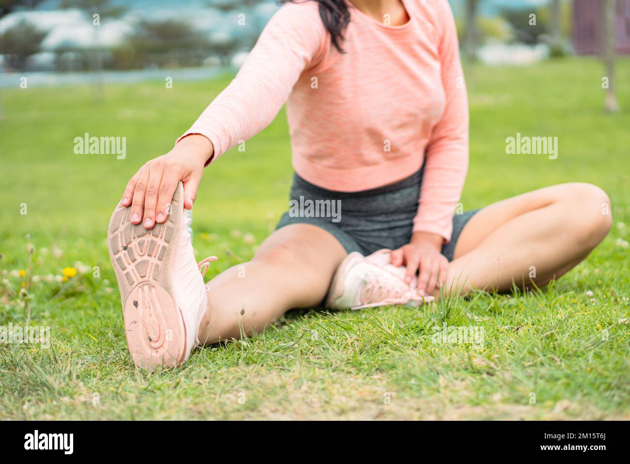 Crop young female in sportswear and sneakers sitting on grass while ...