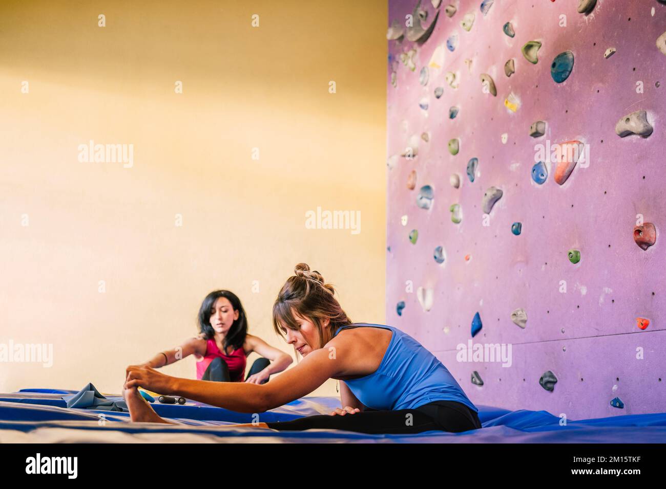 Female athletes stretching arm and legs while sitting on soft mat near ...