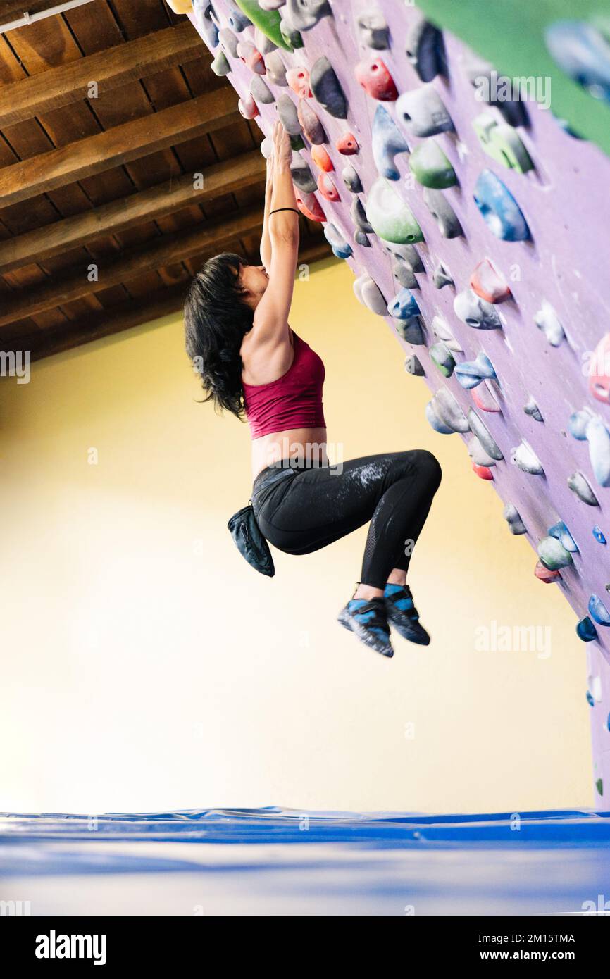 From below full body sportswoman in activewear hanging on grips of ...