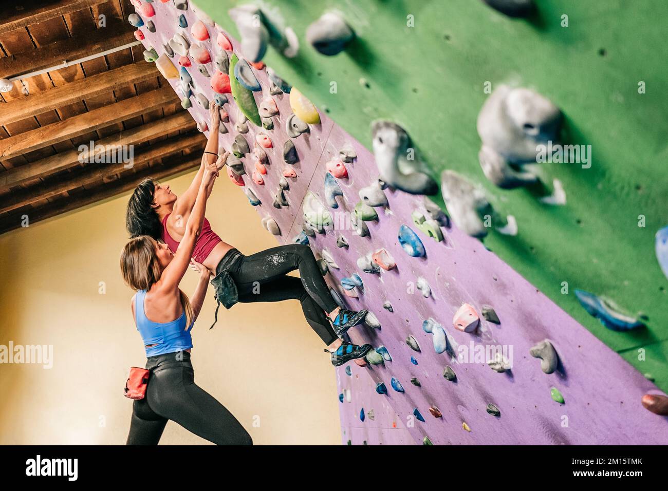 Female coach supporting climber on wall and pointing up during ...