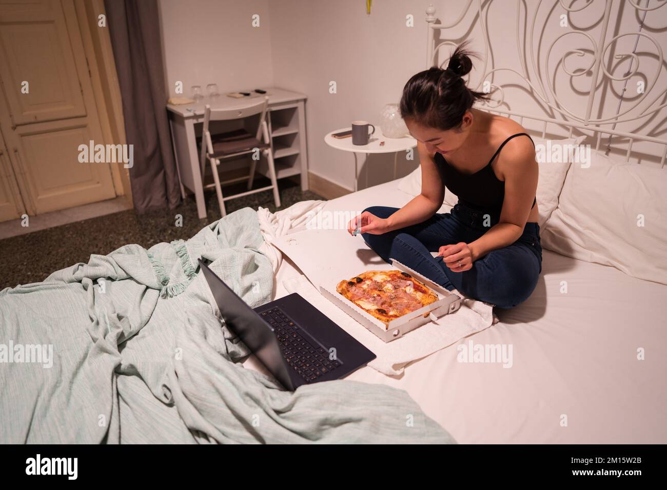 High angle of ethnic female in homey clothes sitting on bed with ...