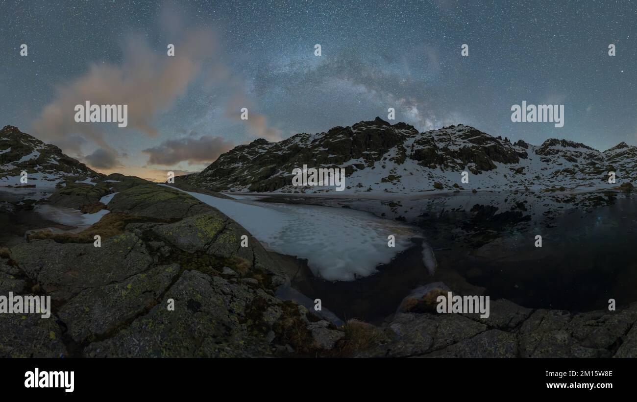 Frozen lake water with snow covered shoreline and dark rocky mountains ...