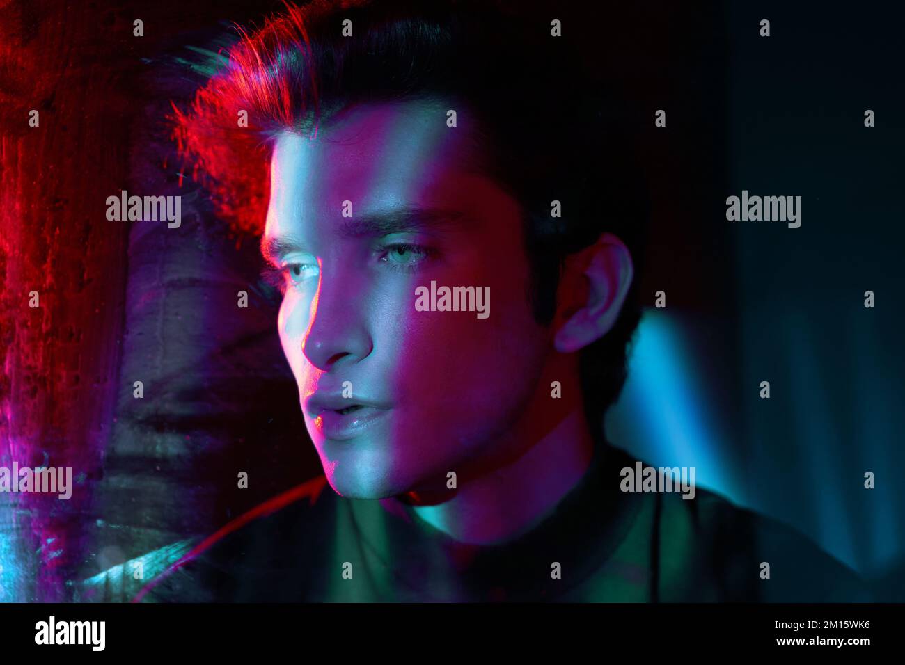 Male model standing in dark studio with glowing colorful neon lights ...