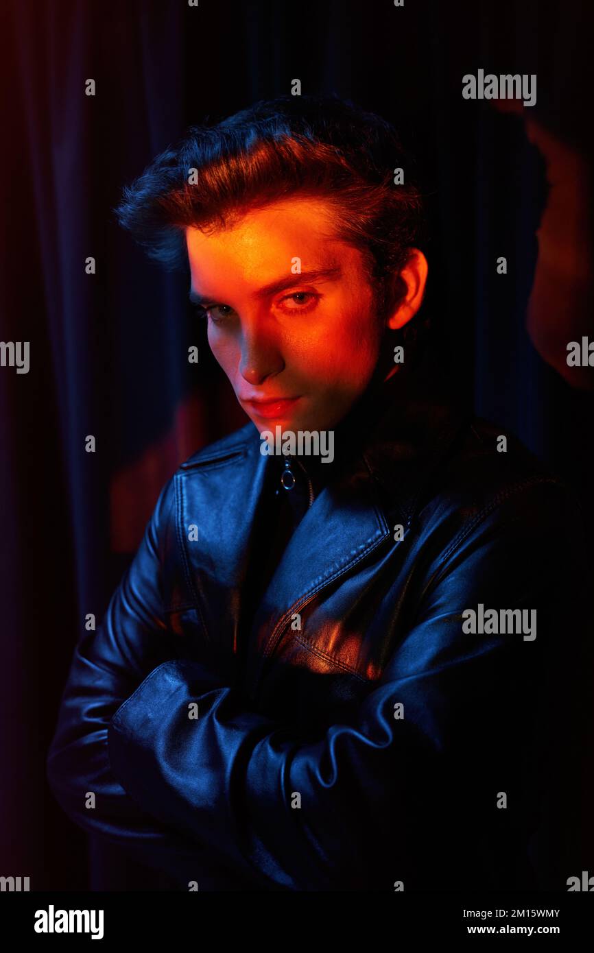 Male model standing with arms crossed in dark studio with glowing red ...