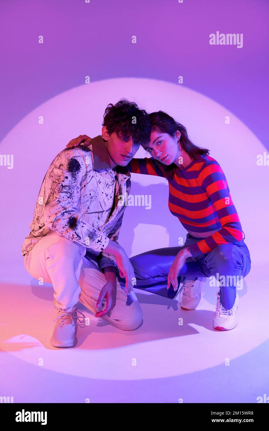 Full body of young models in colorful outfits sitting on haunches and ...