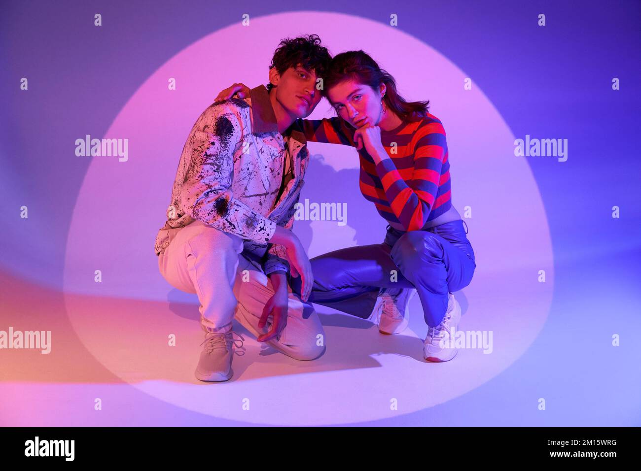 Full body of young models in colorful outfits sitting on haunches and ...