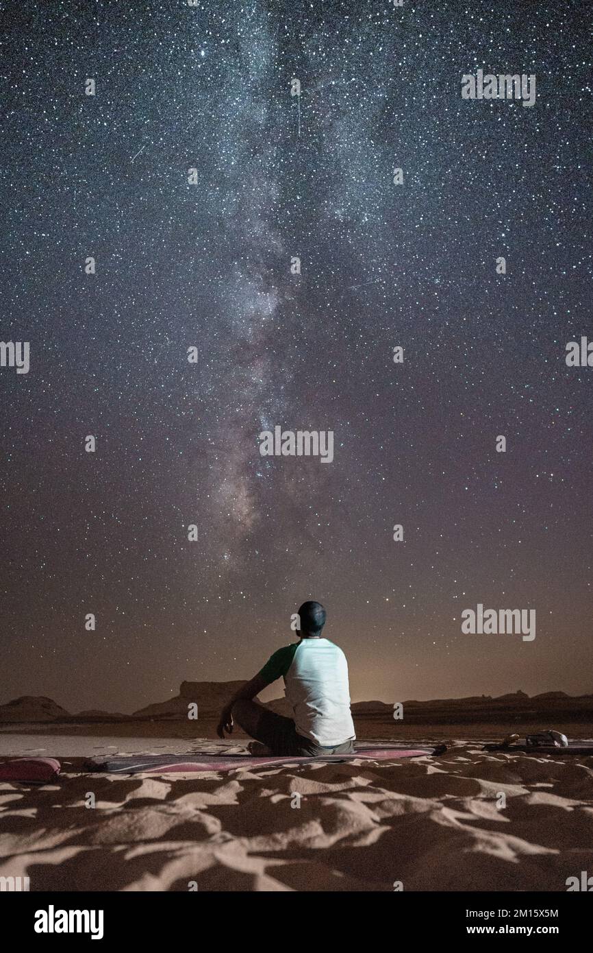 Back view of anonymous black male sitting on sandy ground in Egypt and ...
