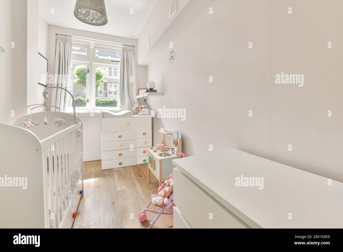 Interior of a room with a wooden crib next to a bright window and white ...