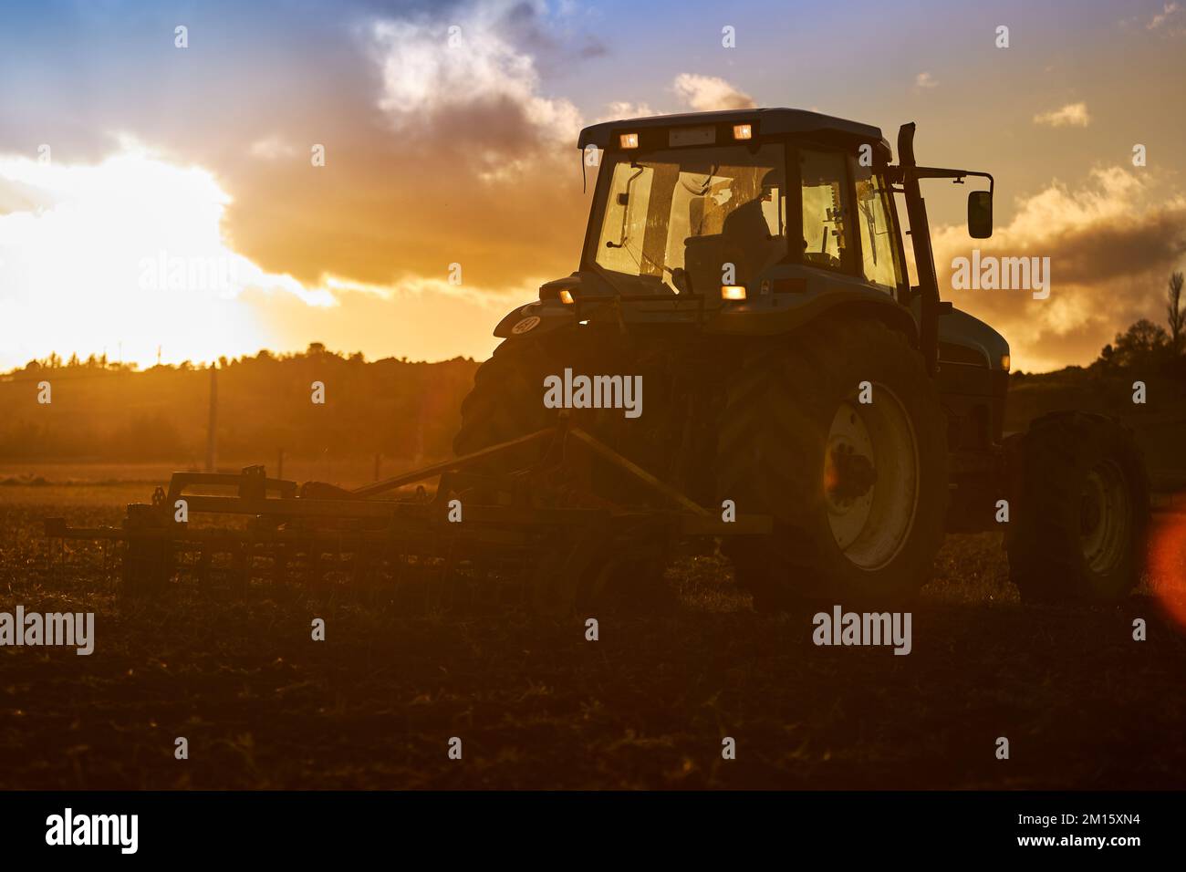 Side view of unrecognizable farmer driving tractor while working soil ...