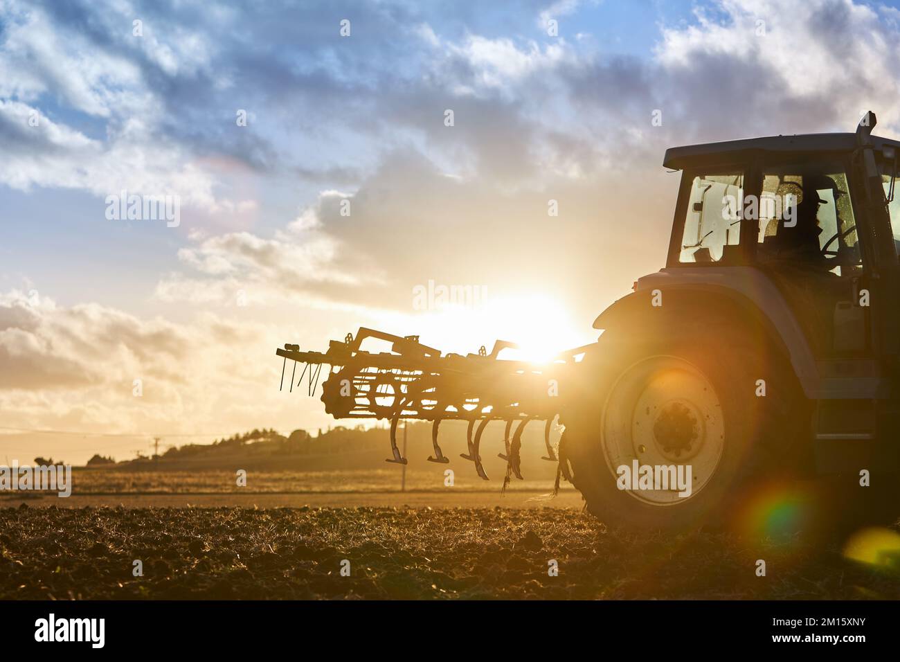 Side view of unrecognizable farmer driving tractor while working soil ...