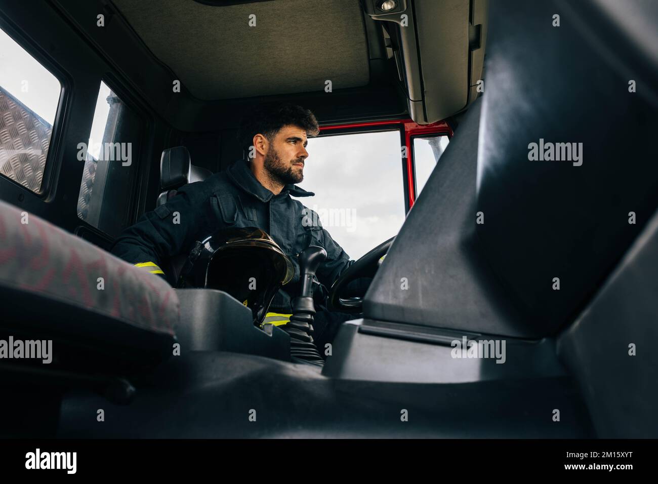 From below serious fireman with helmet sitting on driver seat of fire ...