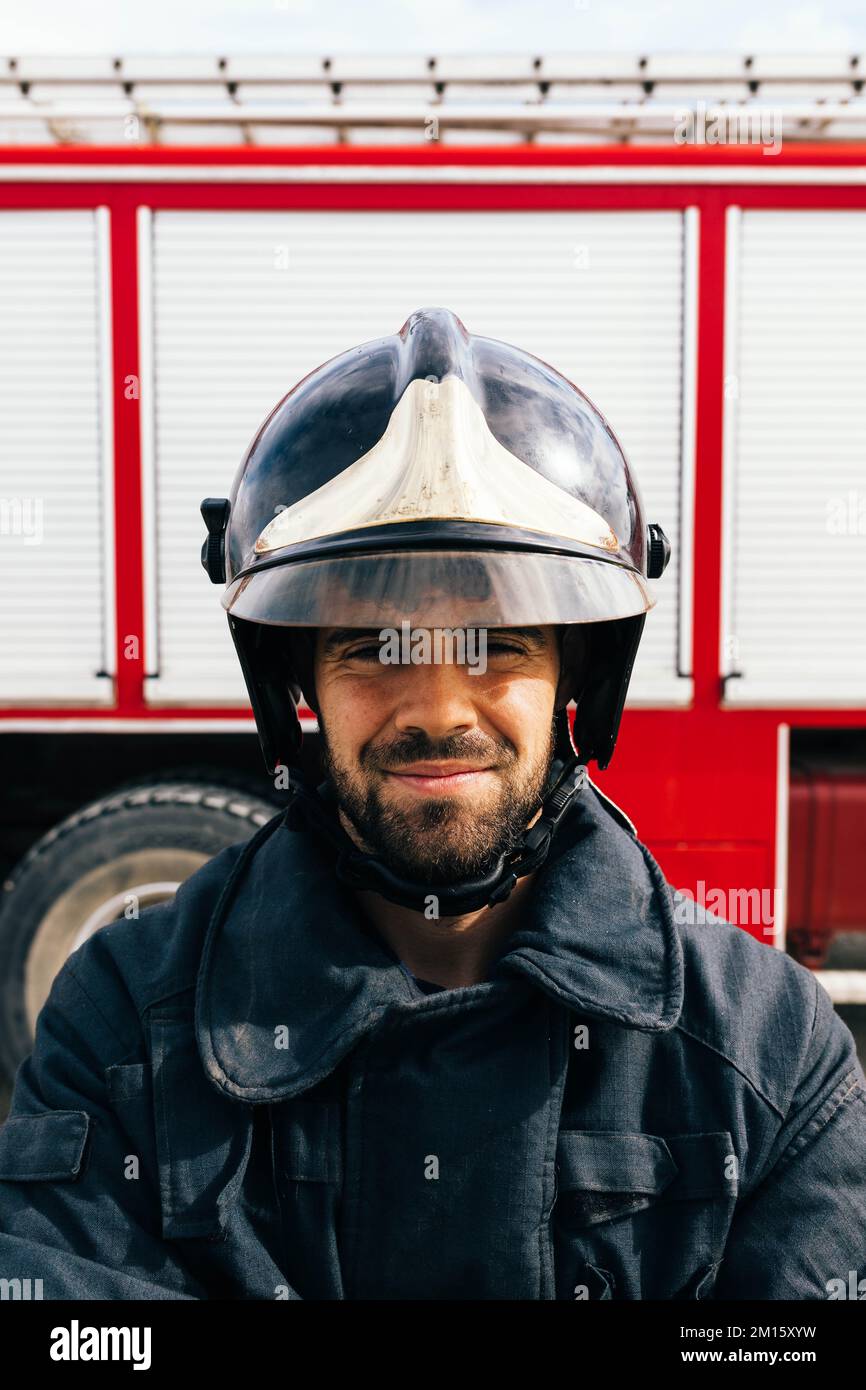 Positive Hispanic fireman in protective uniform looking at camera with ...