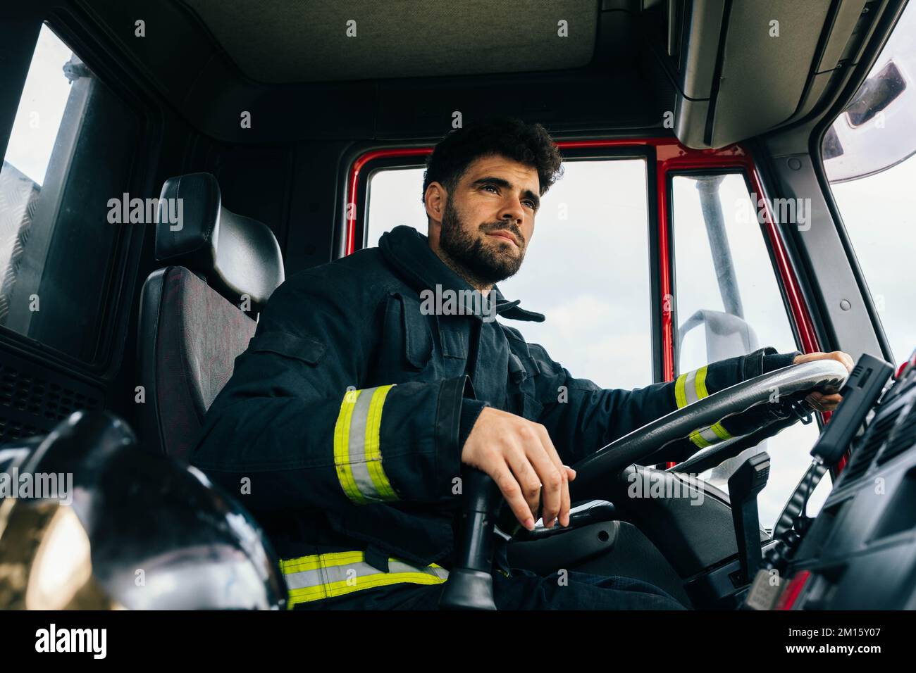 From below serious fireman with helmet sitting on driver seat of fire ...