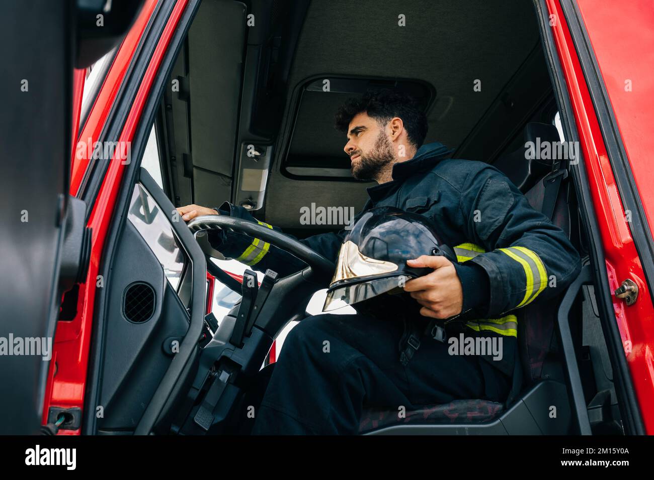 From below serious fireman with helmet sitting on driver seat of fire ...