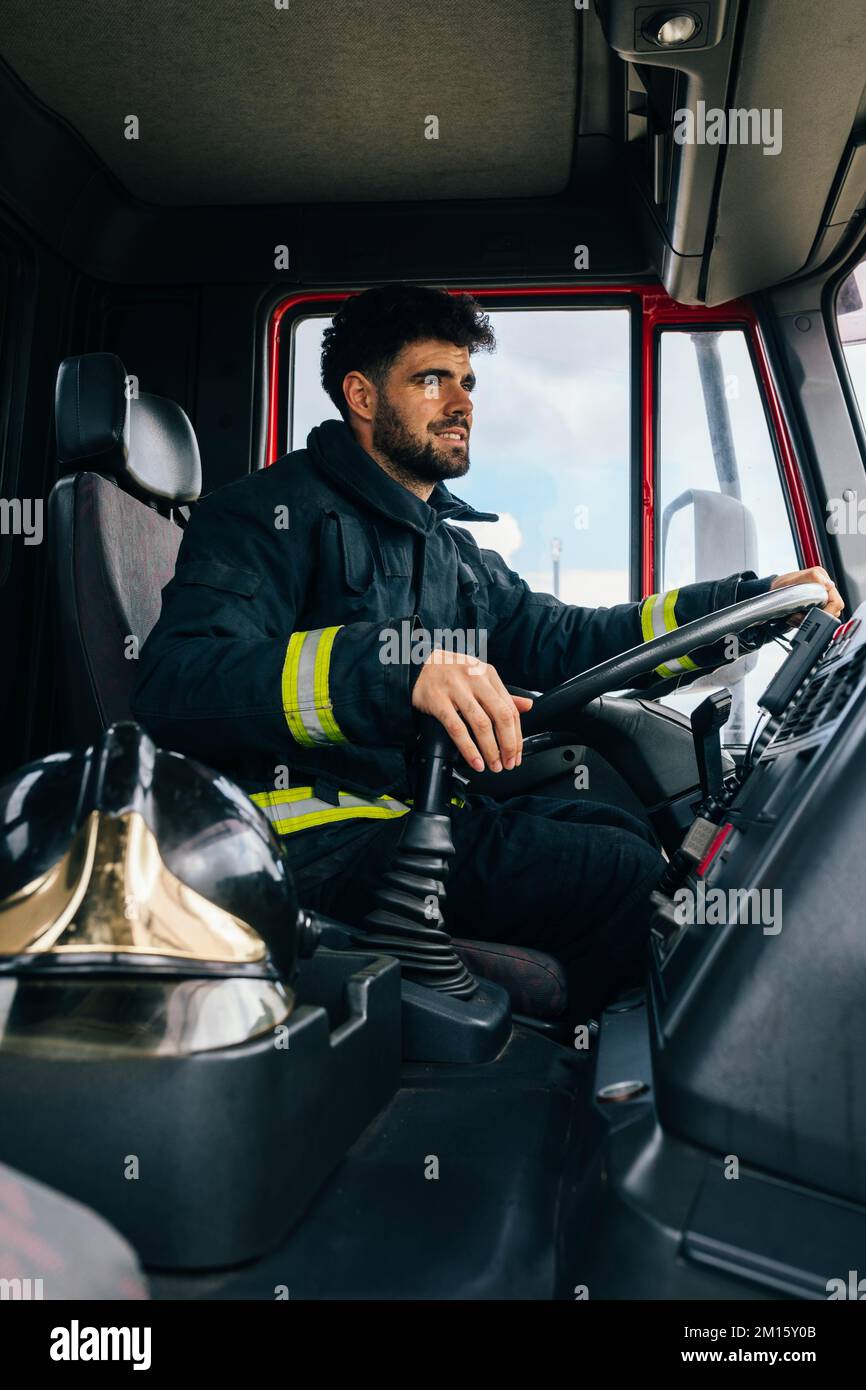 Fireman with helmet sitting on driver seat of fire engine during work ...