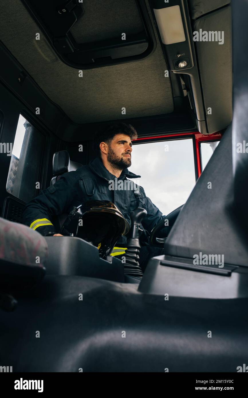 From below serious fireman with helmet sitting on driver seat of fire ...