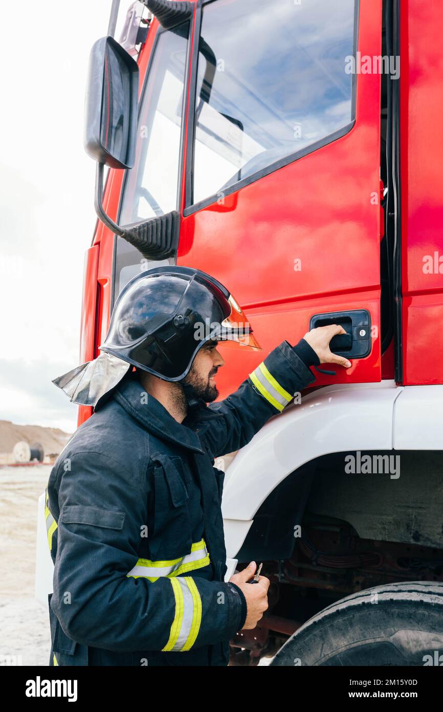 Side view of bearded fireman in protective uniform and helmet opening ...