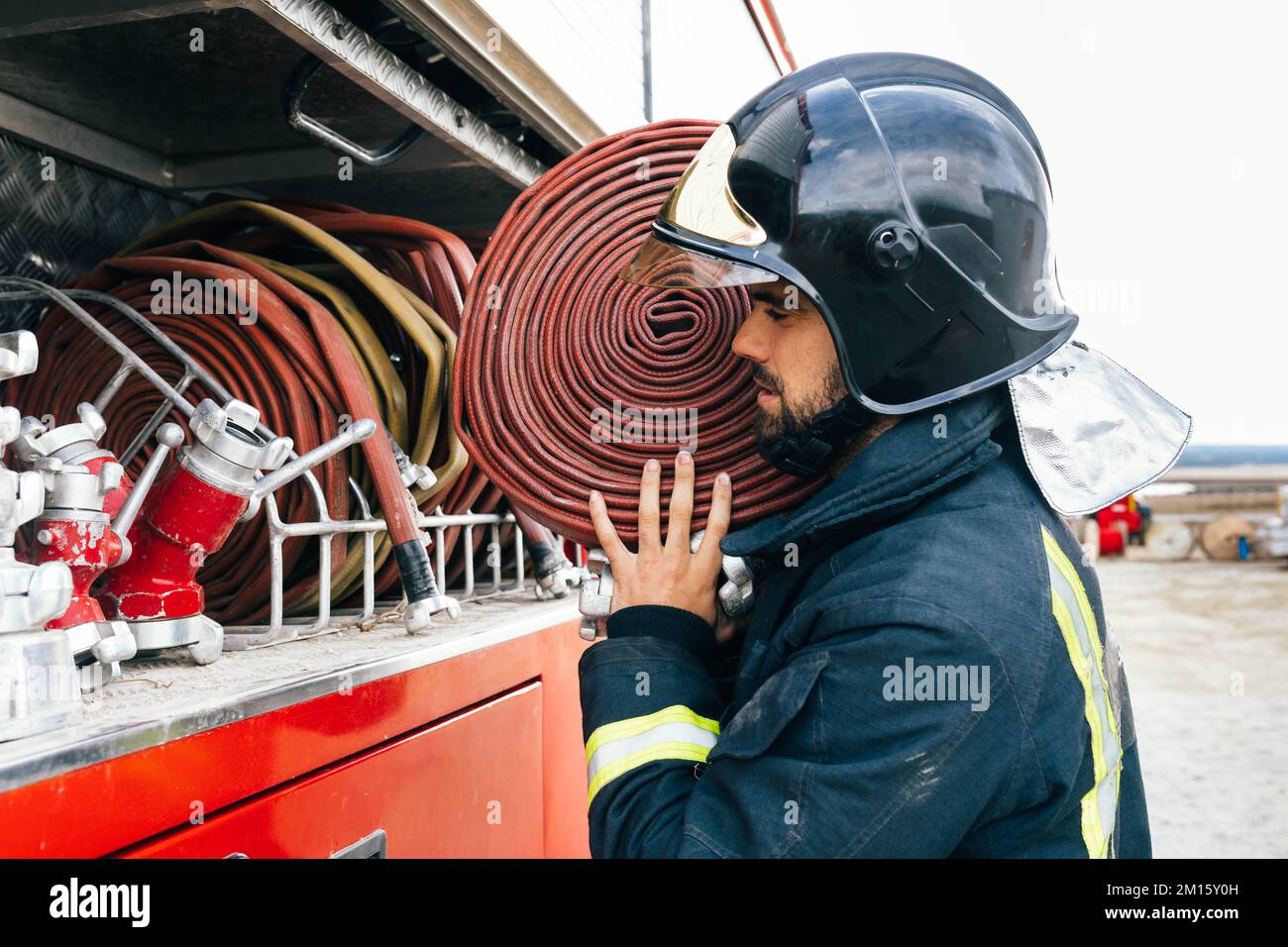Side view of Hispanic firefighter in uniform and helmet carrying hose ...