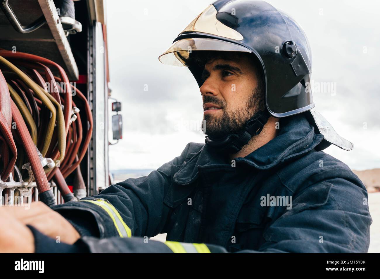 Side view of focused fireman in workwear and helmet putting rolled up ...
