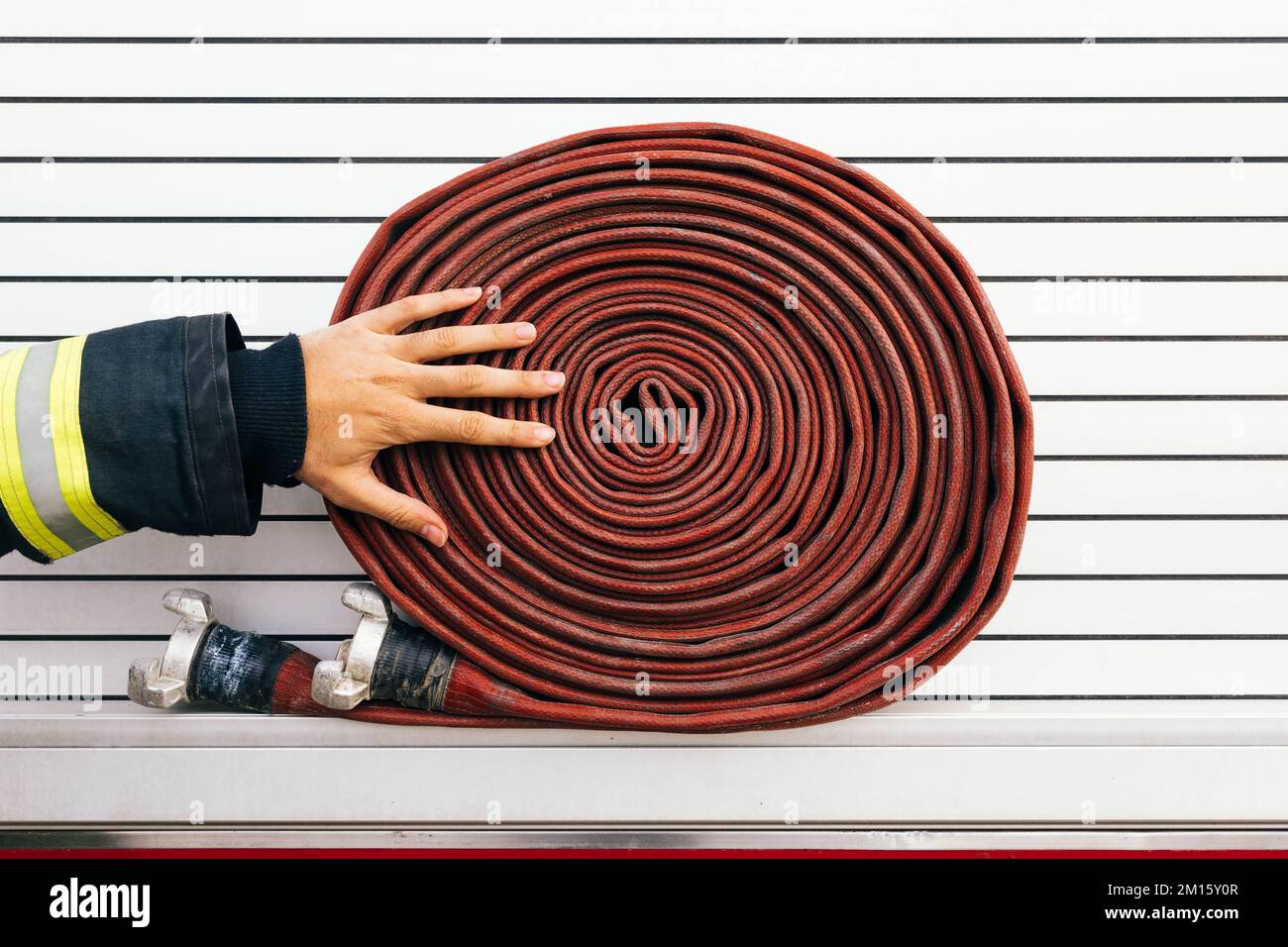 Anonymous fireman in protective workwear touching rolled up hose placed ...