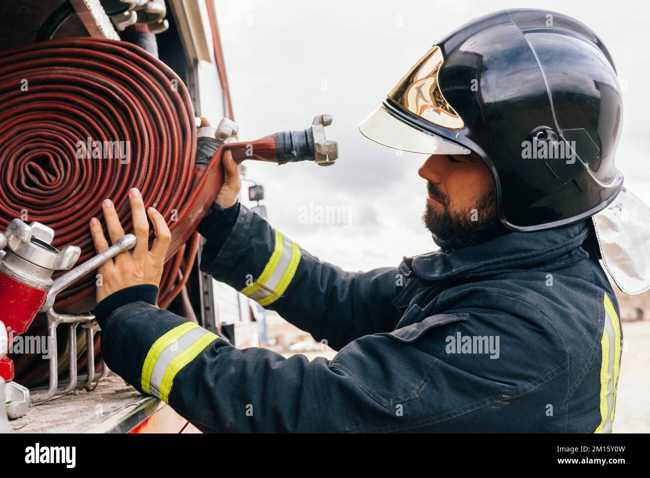 Side view of focused fireman in workwear and helmet putting rolled up ...