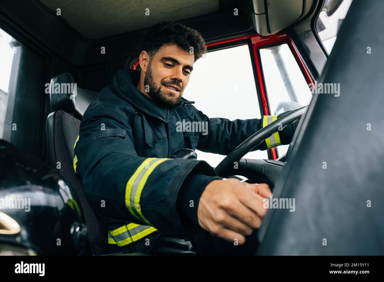 Side view bearded Hispanic firefighter pressing button on dashboard and ...