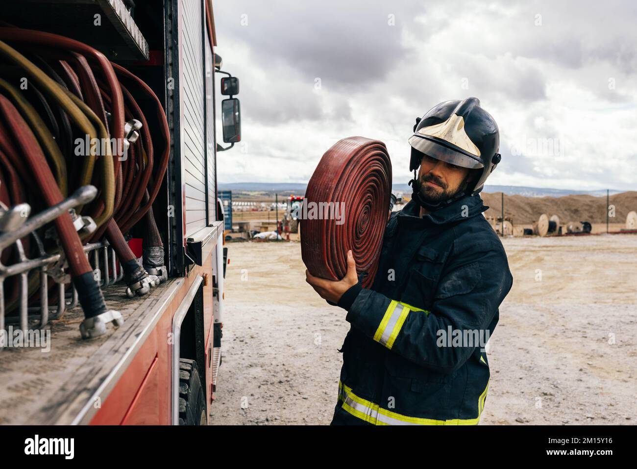 Side view of Hispanic firefighter in uniform and helmet carrying hose ...