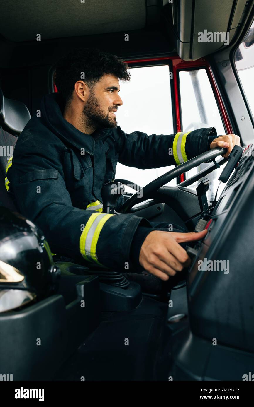 Side view bearded Hispanic firefighter pressing button on dashboard and ...