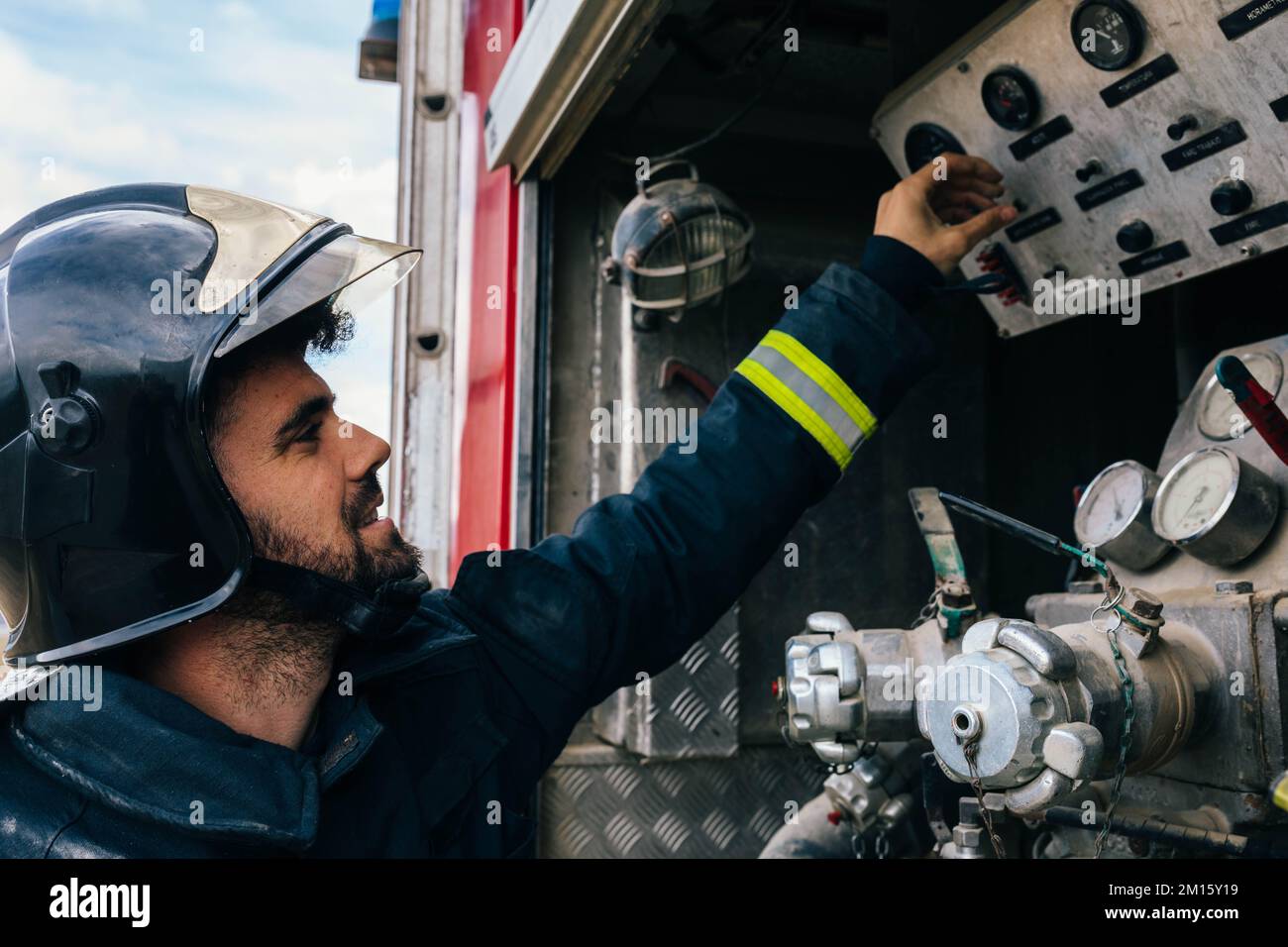 Bearded male firefighter in uniform and helmet touching switch on ...