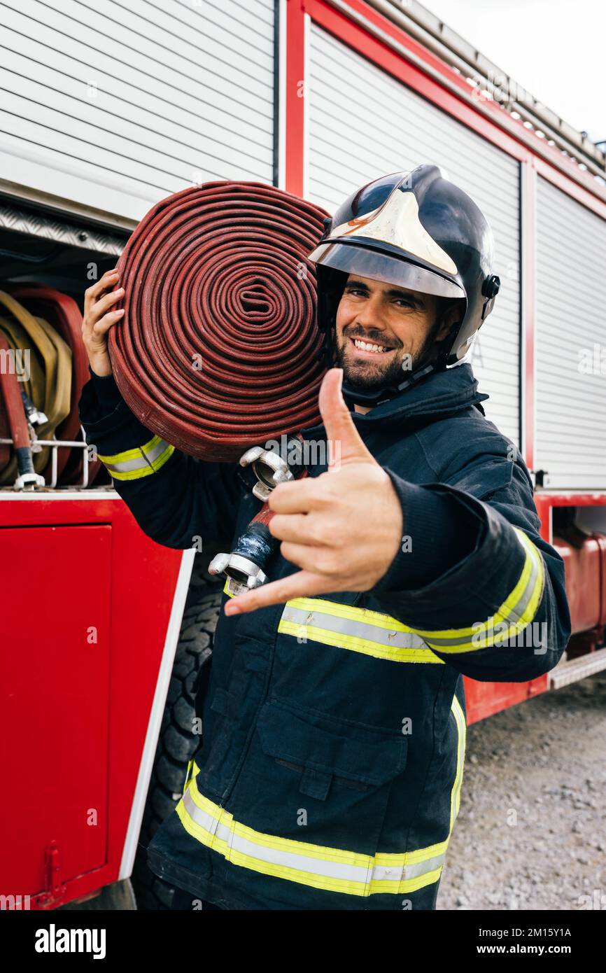 Happy Hispanic firefighter in uniform and helmet carrying hose on ...