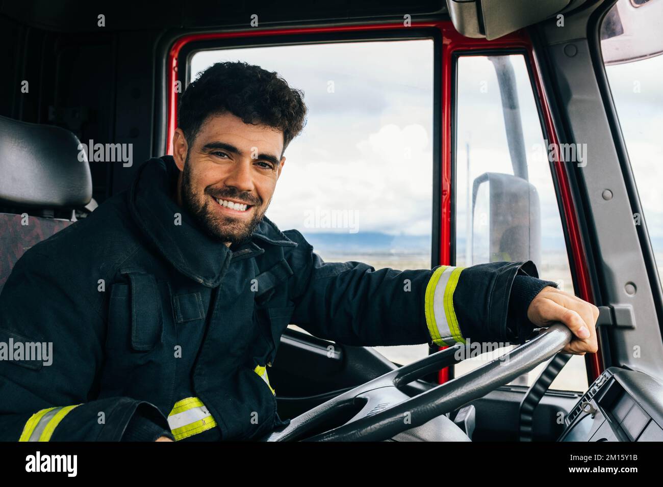 Happy Hispanic firefighter in protective uniform smiling and looking at ...