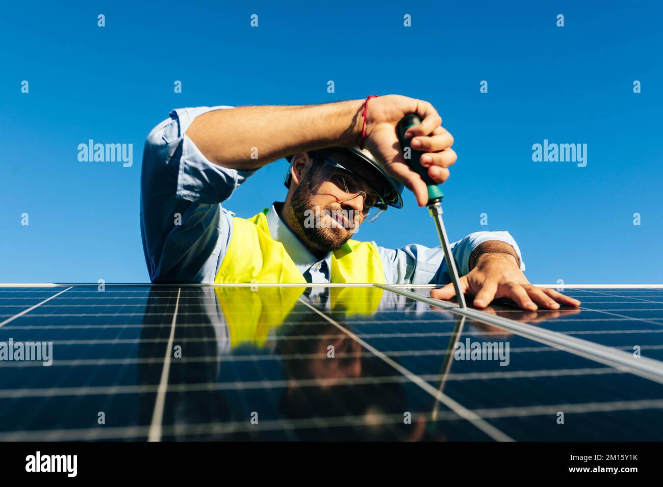 Low angle of bearded worker in protective helmet with screwdriver ...