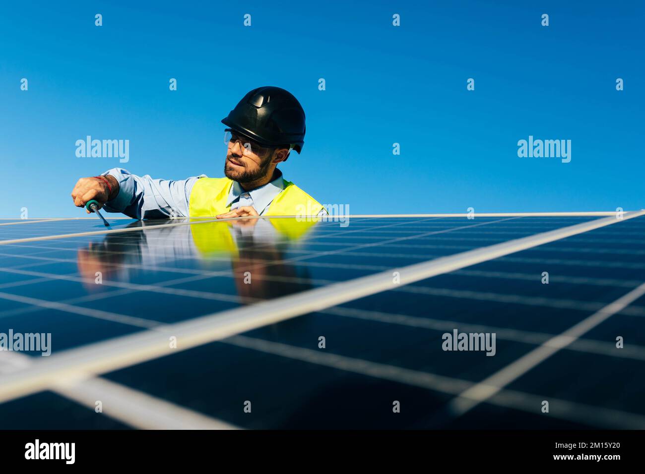 Low angle of bearded worker in protective helmet with screwdriver ...