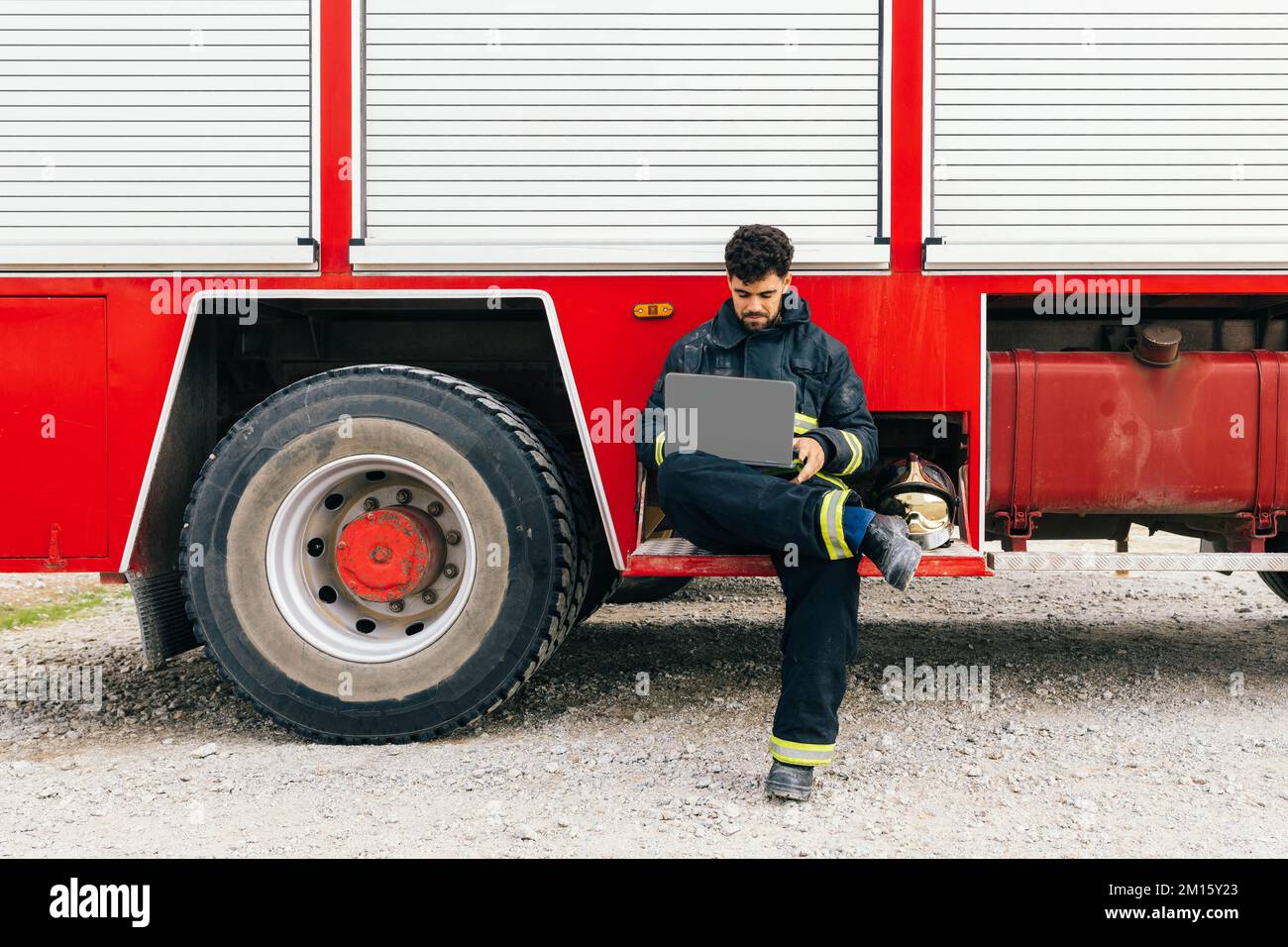 Full body focused Hispanic firefighter in uniform sitting on step ...