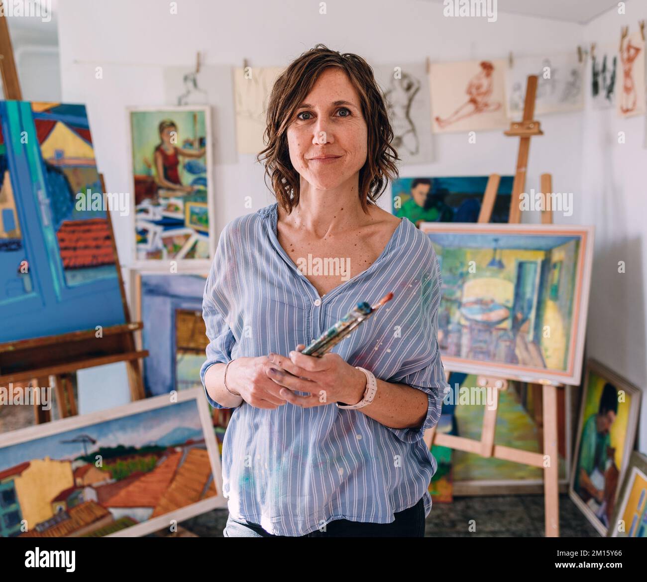 Positive female painter in casual clothes holding paintbrush while ...