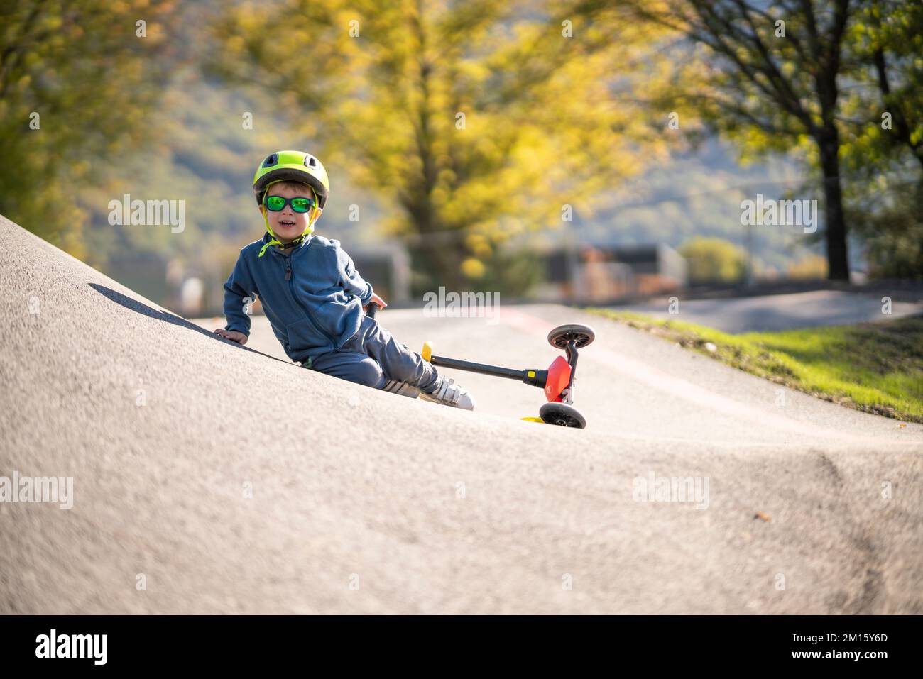 Full body little boy in helmet and goggles lying on asphalt slope near ...