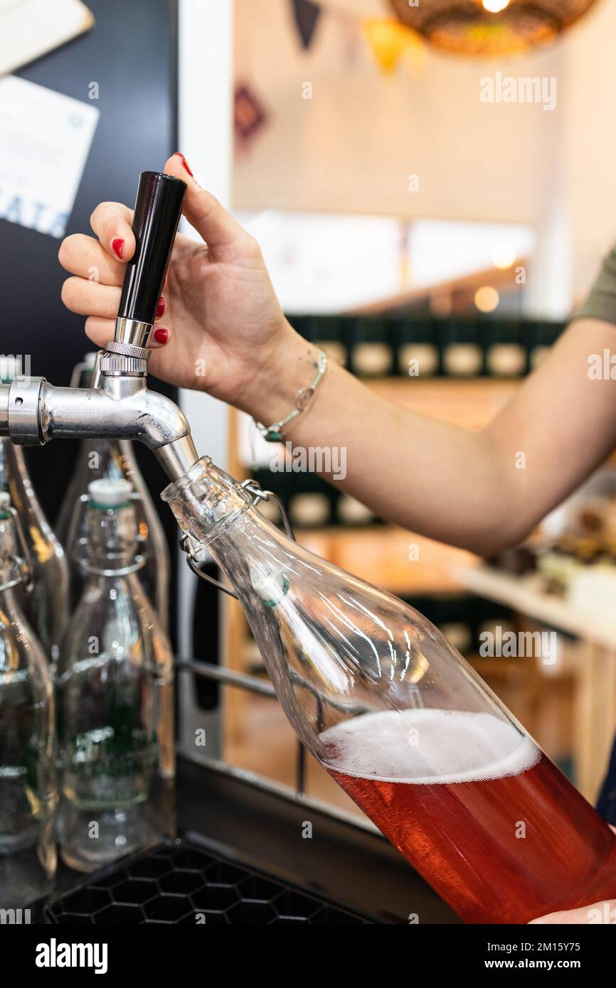 Crop anonymous person pouring fresh beverage into glass bottle from ...