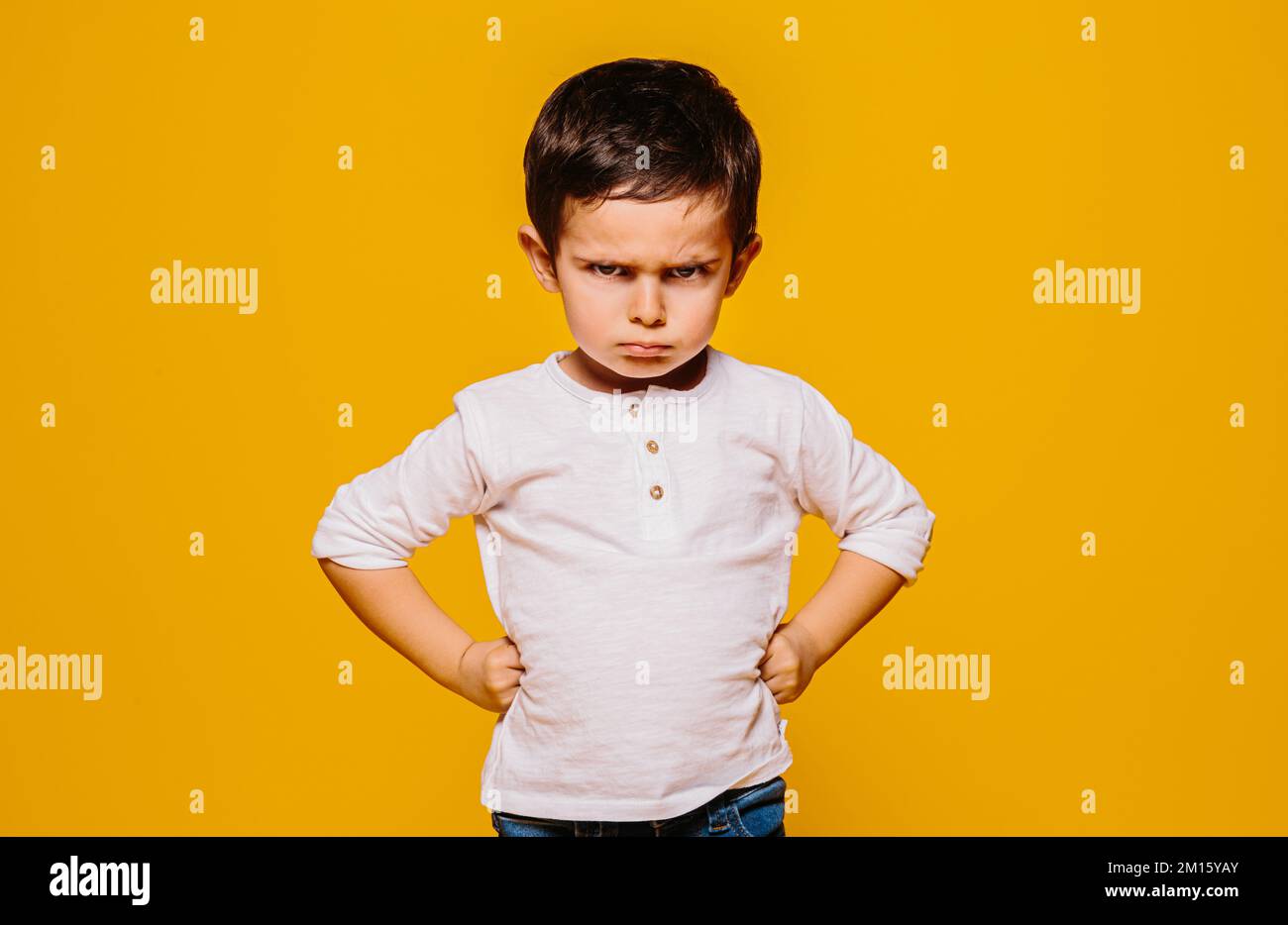 Cute little boy in white shirt looking at camera with angry expression ...