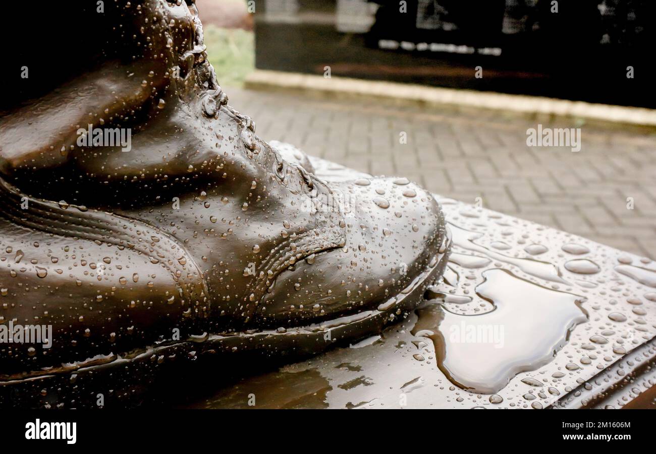 A closeup shot of rain droplets on the boot of a bronze memorial statue ...