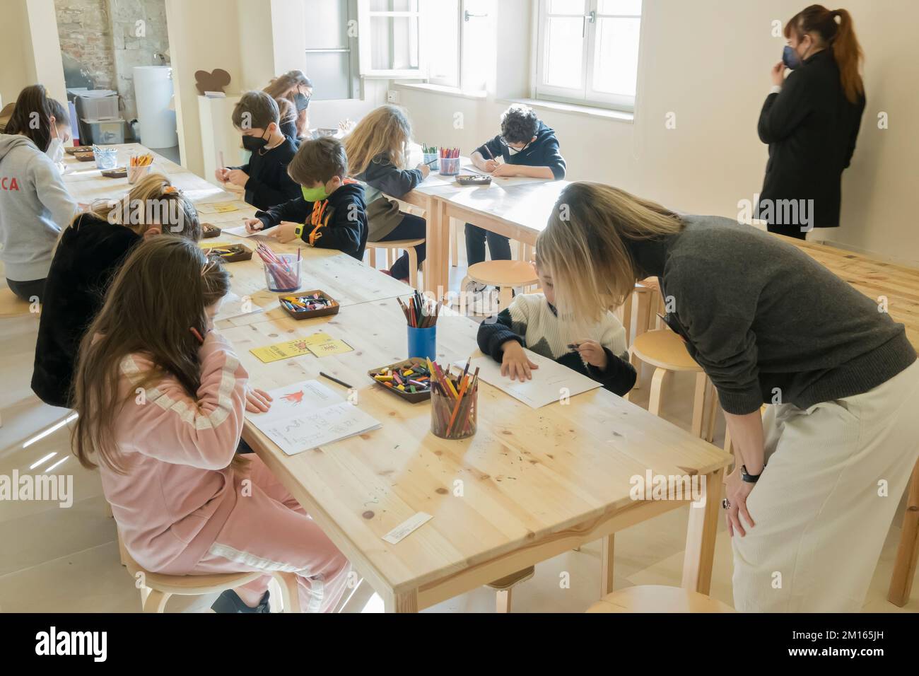 School kids with a teacher in the classroom. Kids are busy drawing ...