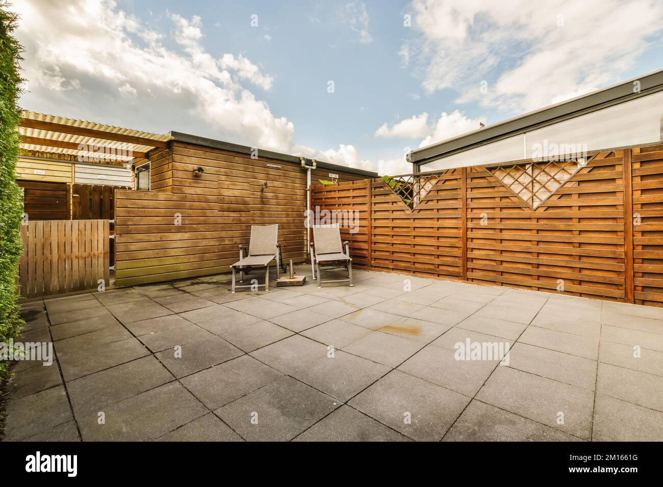 a backyard area with wooden fences and white clouds in the blue sky above it is an empty chair ...