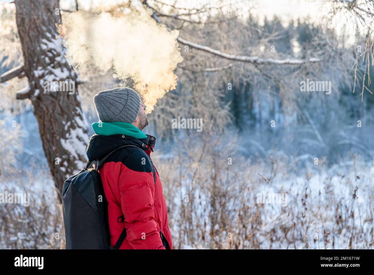 a man in the winter in the cold exhales a cloud of steam, smoke ...