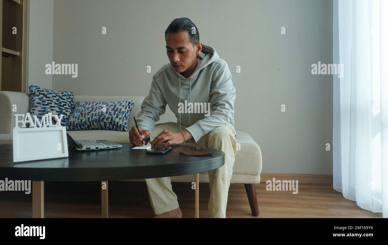 Man writing on paper work while working from home using laptop and ...