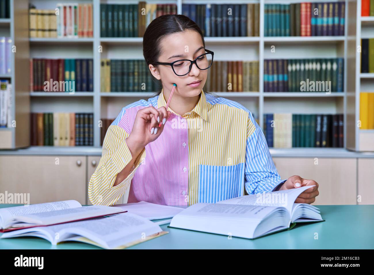 Teenage girl student looking at book, studying in library Stock Photo ...