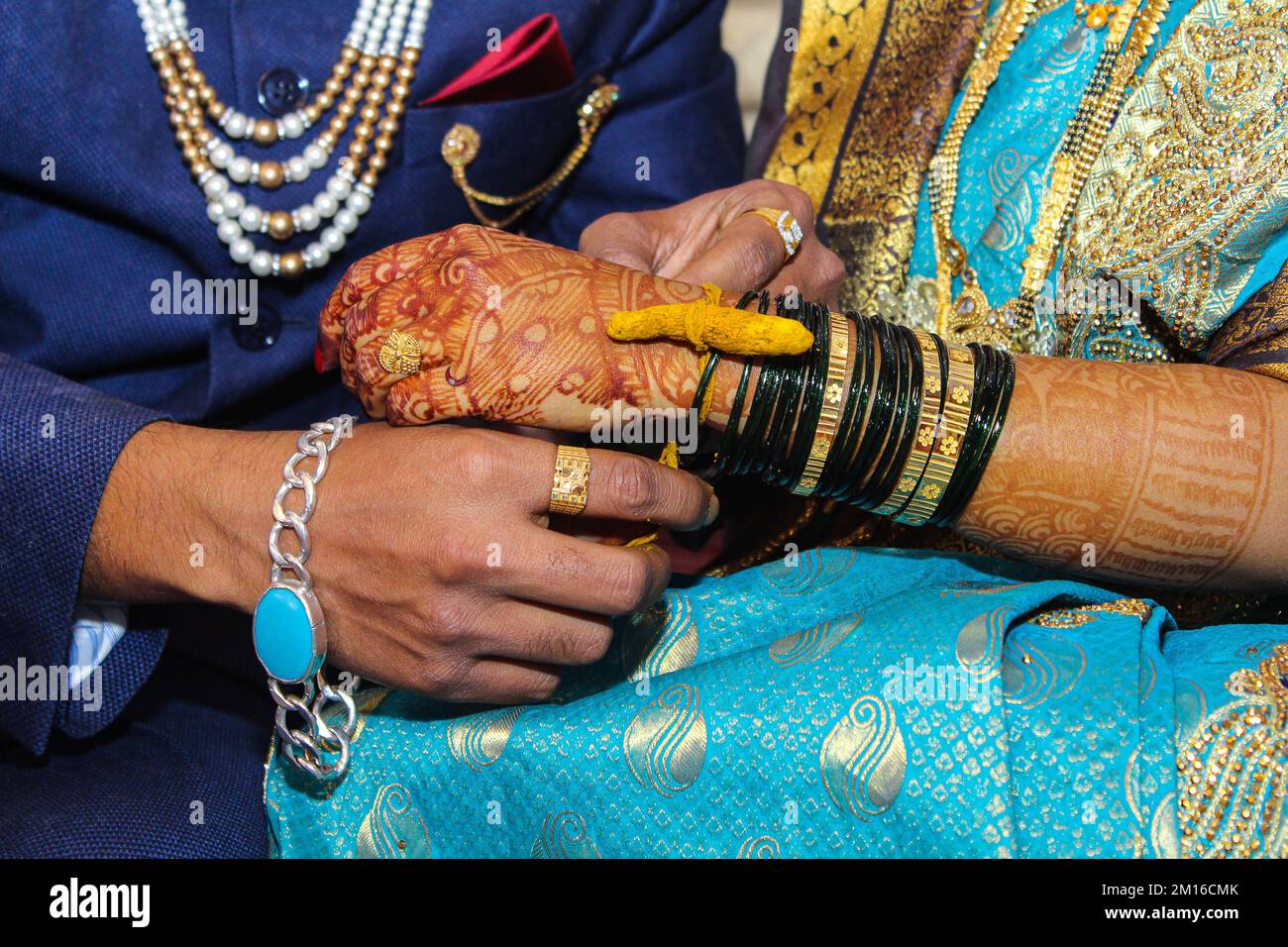 An Indian groom tying raw turmeric band to bride's hand during Hindu ...